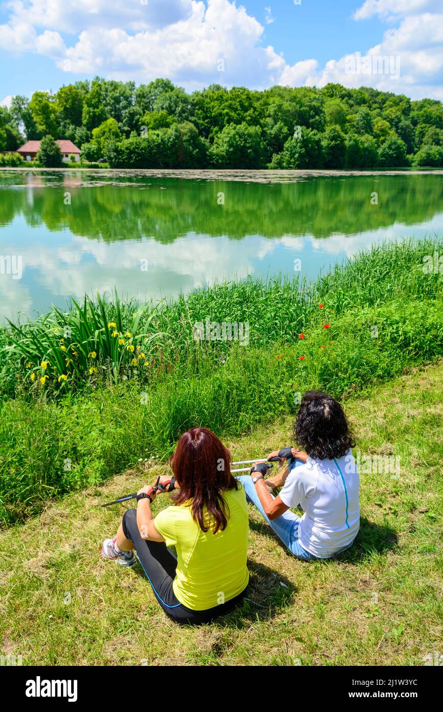 Two sporty women doing pause during a Nordic walking exercise by a ...