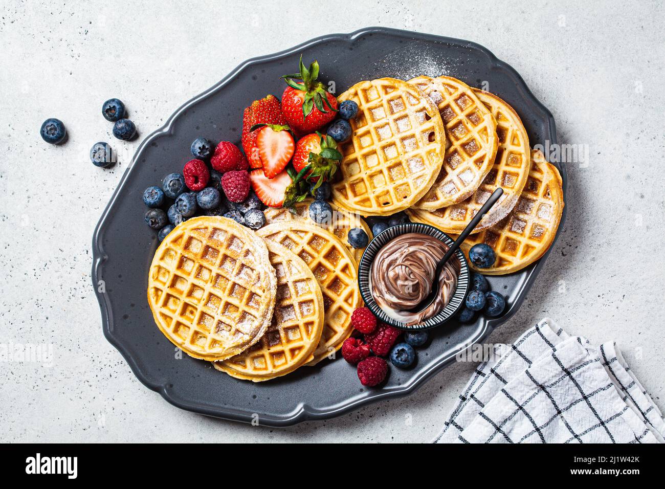 Homemade waffles with berries and chocolate cream on a dark plate, gray ...