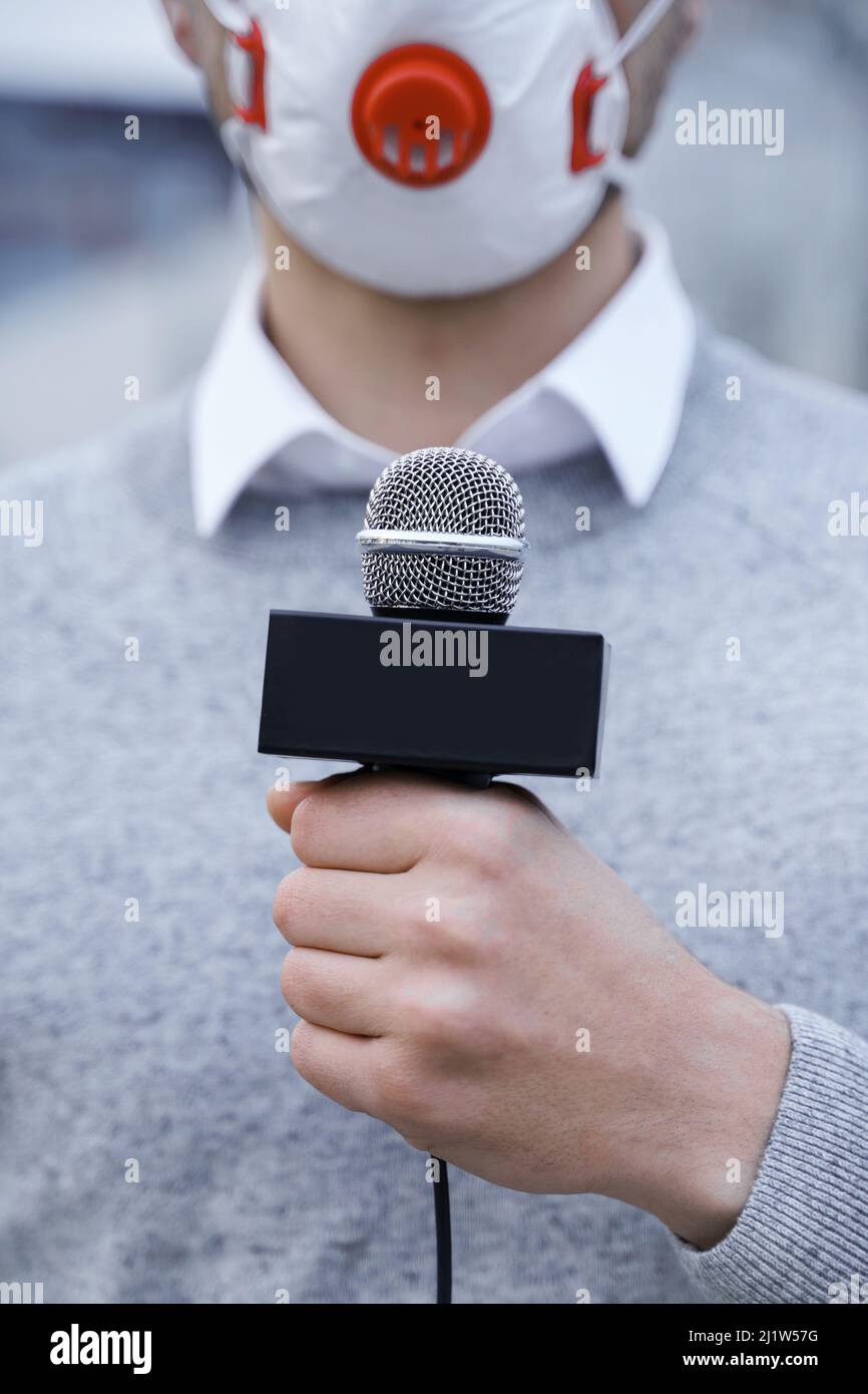 News reporter wearing a prevention mask and speaking into a microphone ...