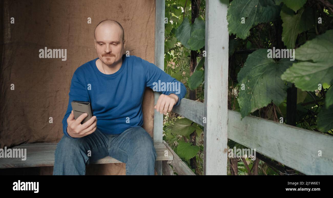 Man communicates online using his phone while sitting on porch of ...