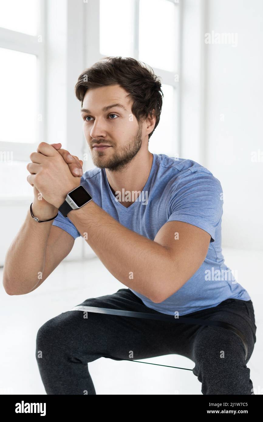 Man doing squats with a loop resistance band during workout in the gym ...