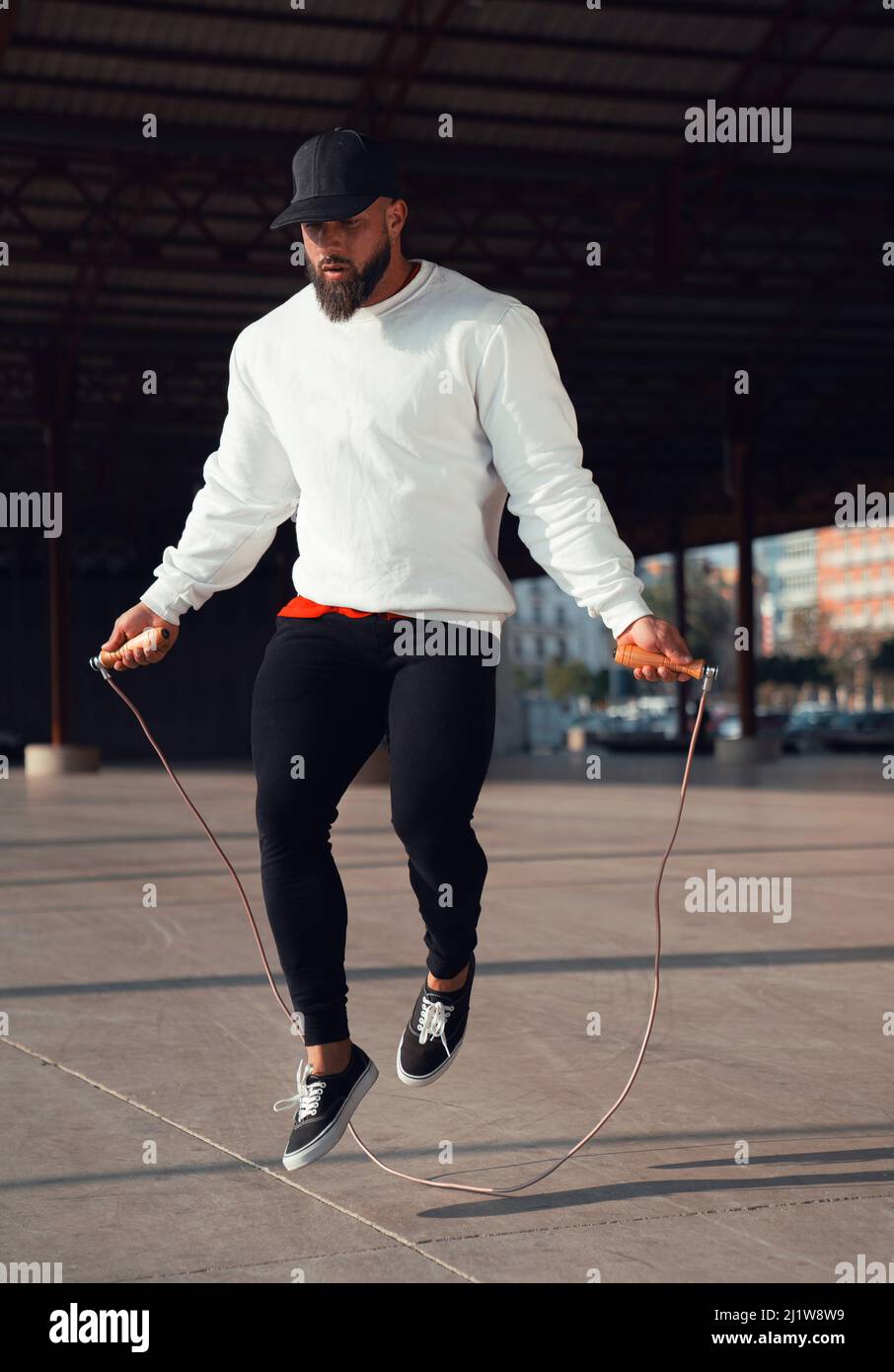 Full body of active bearded male in black cap jumping rope while ...