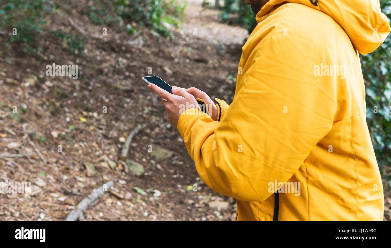 Side view crop male hiker in yellow jacket surfing cellphone while ...