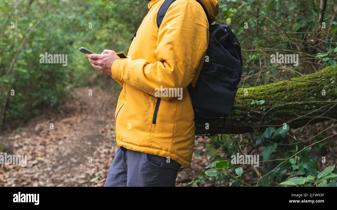 Side view crop male hiker in yellow jacket surfing cellphone while ...