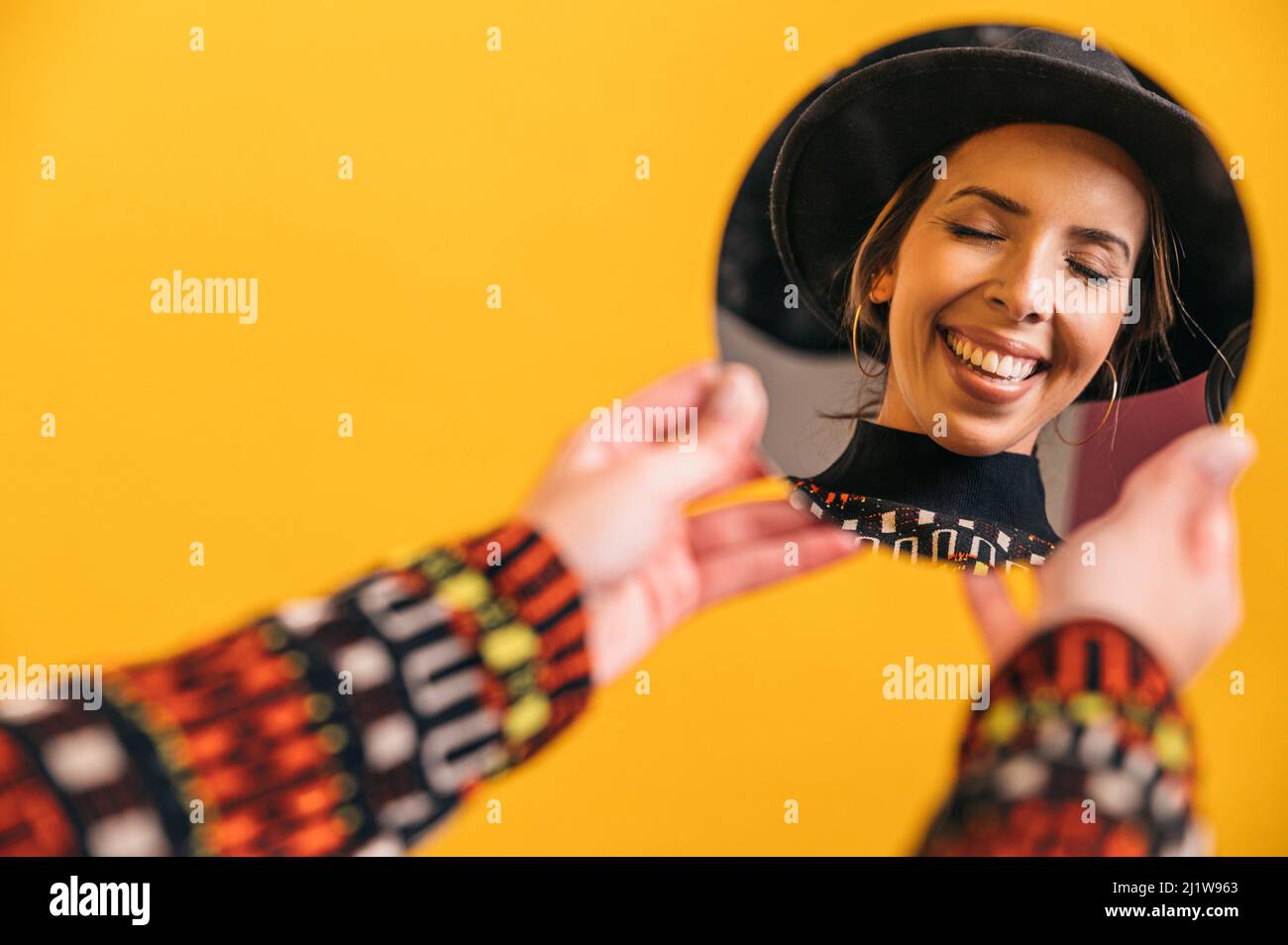 Back view of stylish female in hat reflecting in round shaped mirror ...