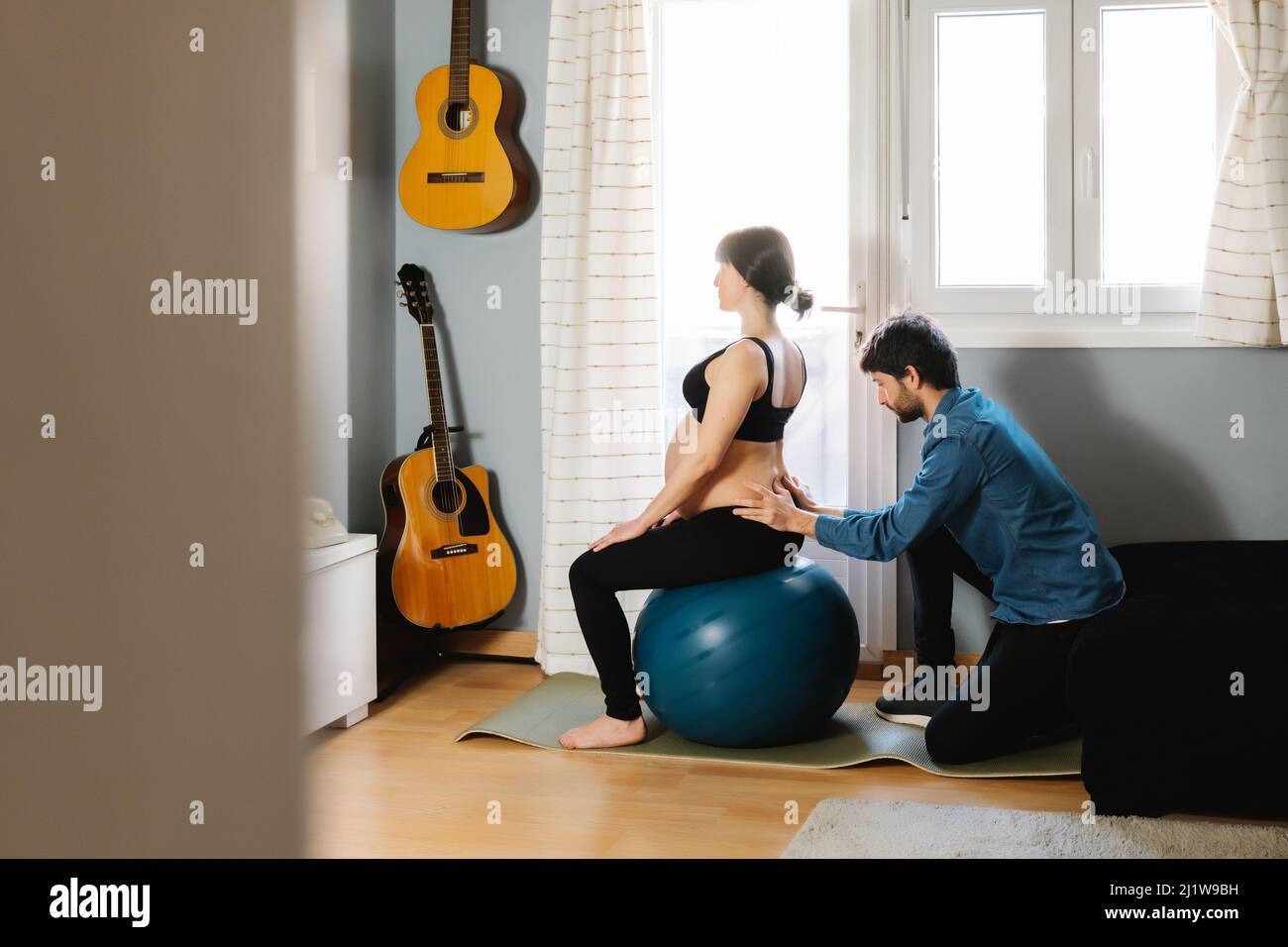 Side view of loving husband helping pregnant wife doing exercise on fit ...