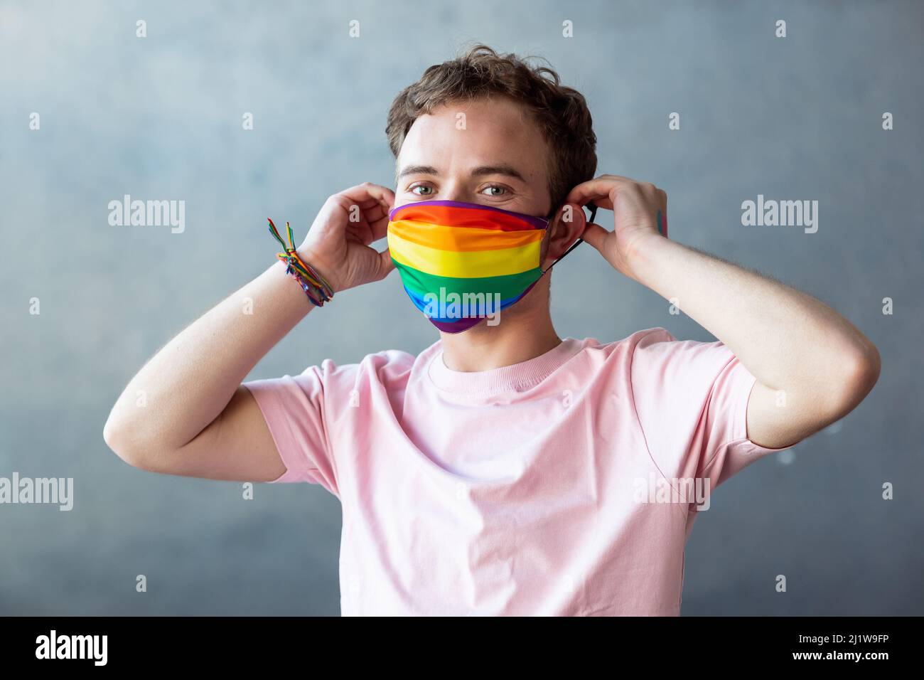 Transgender man looking at camera while putting on protective mask with ...