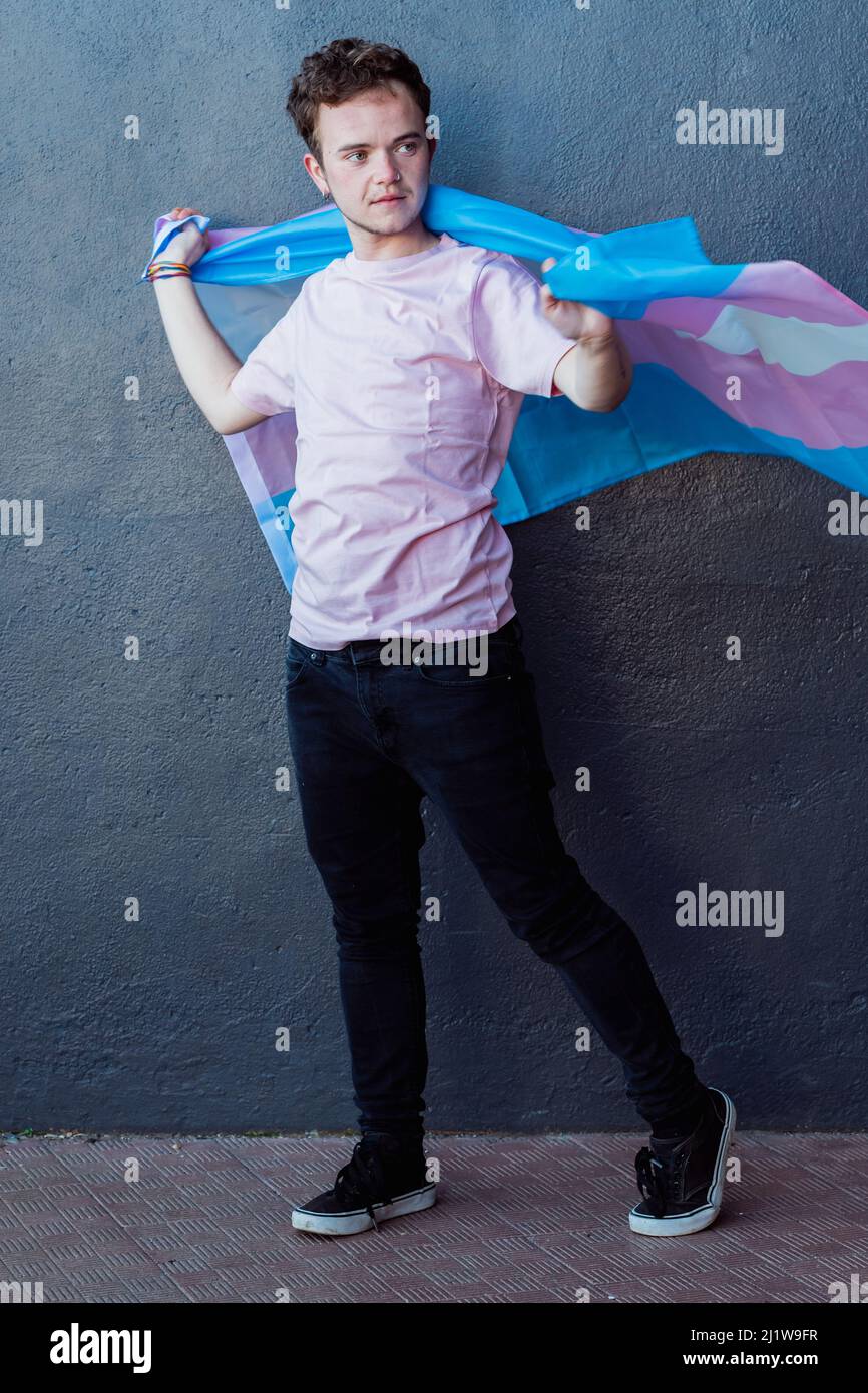 Side view of serious man wrapping with colorful transgender flag with ...