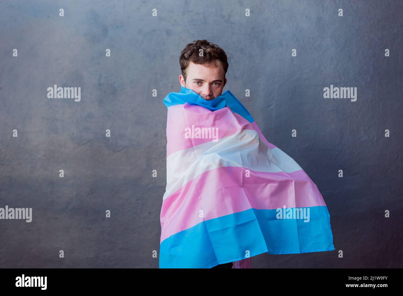 Serious man wrapping with colorful transgender flag with stripes while ...