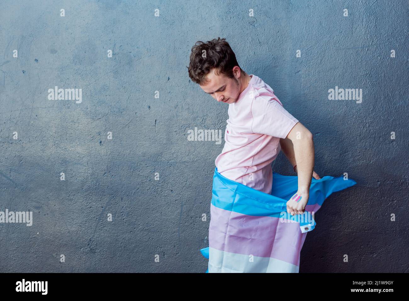 Side view of serious man wrapping with colorful transgender flag with ...