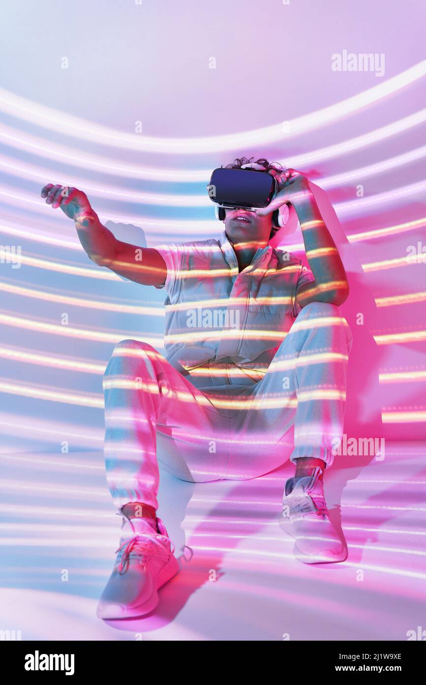 Male in modern VR goggles sitting on white background in studio with ...