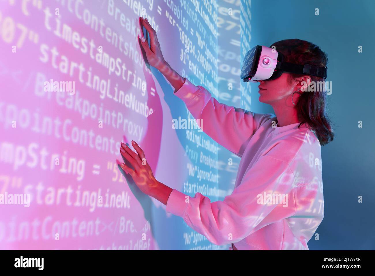 Woman in casual wear and modern black VR goggles touching wall with ...
