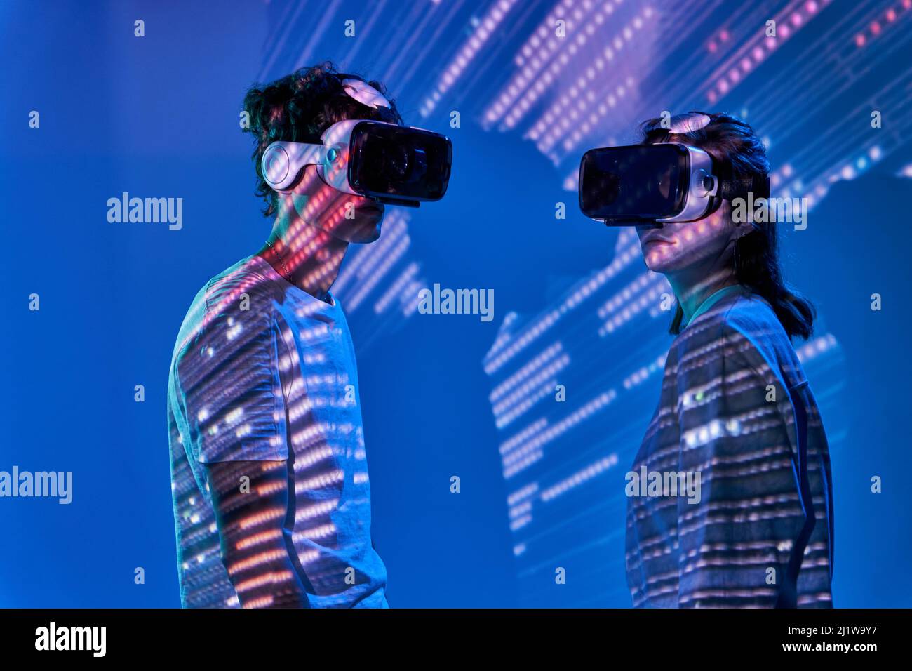 Side view of couple in modern VR goggles while standing on blue ...