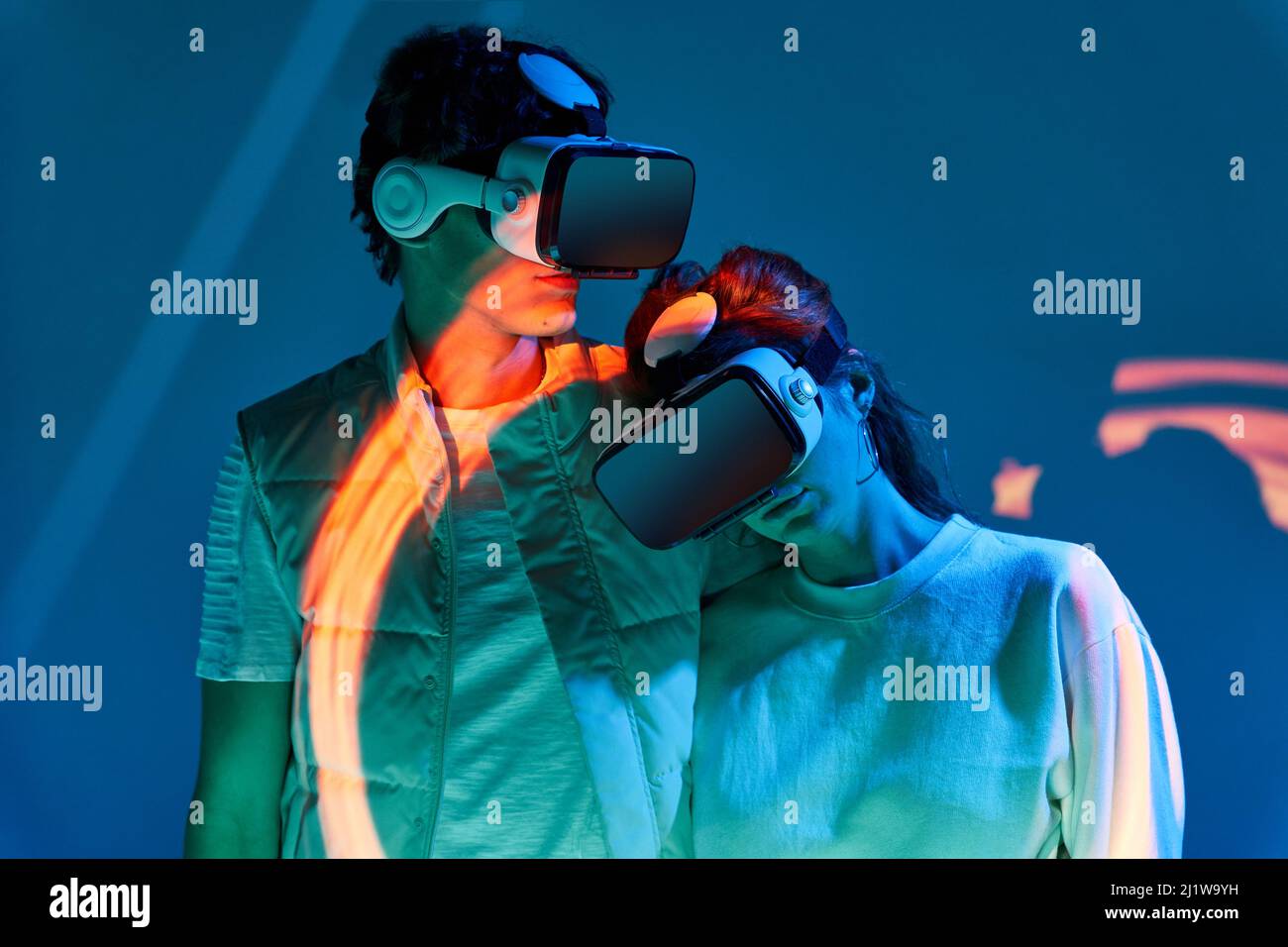 Couple in modern VR goggles standing at wall with glowing lights while ...
