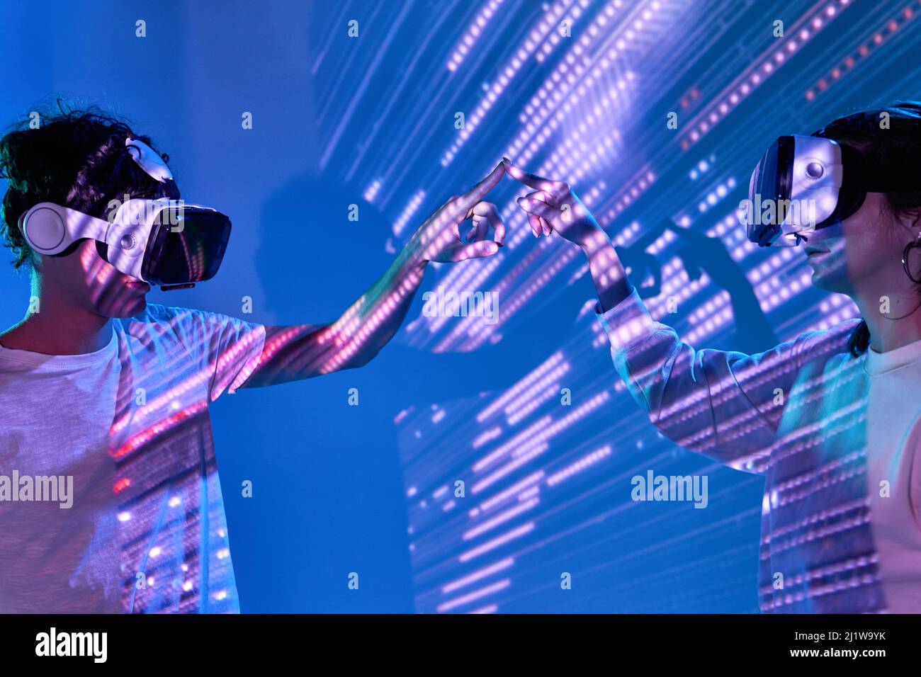 Side view of couple in modern VR goggles touching fingers while ...