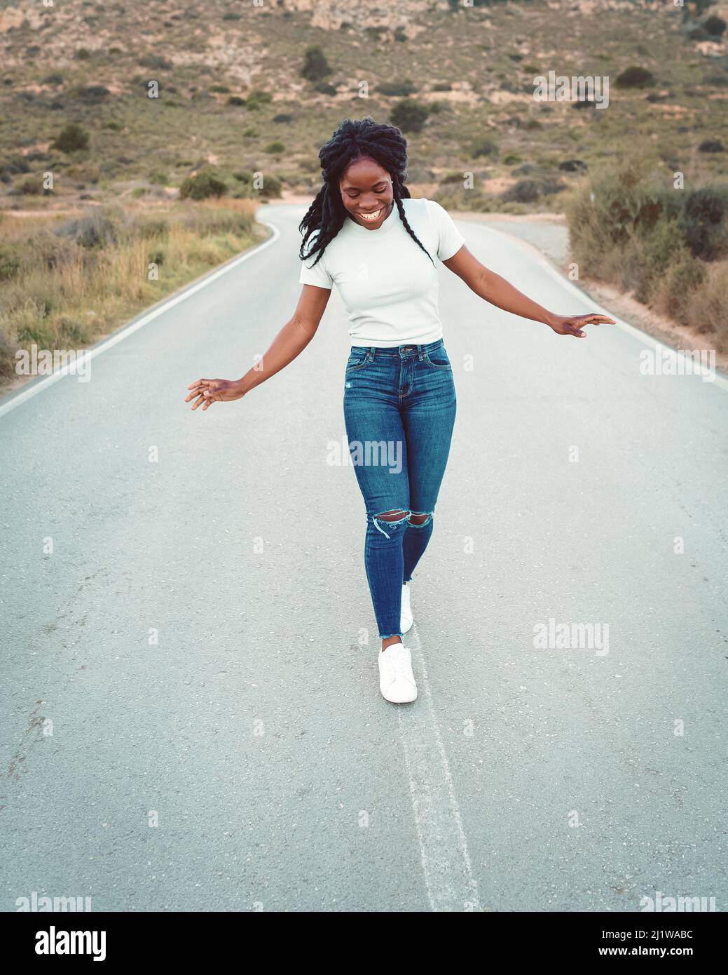 Happy African American female walking along asphalt roadway in ...