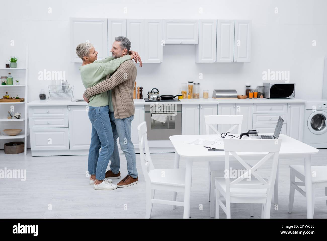 Side view of senior woman hugging husband near papers and devices in kitchen Stock Photo - Alamy