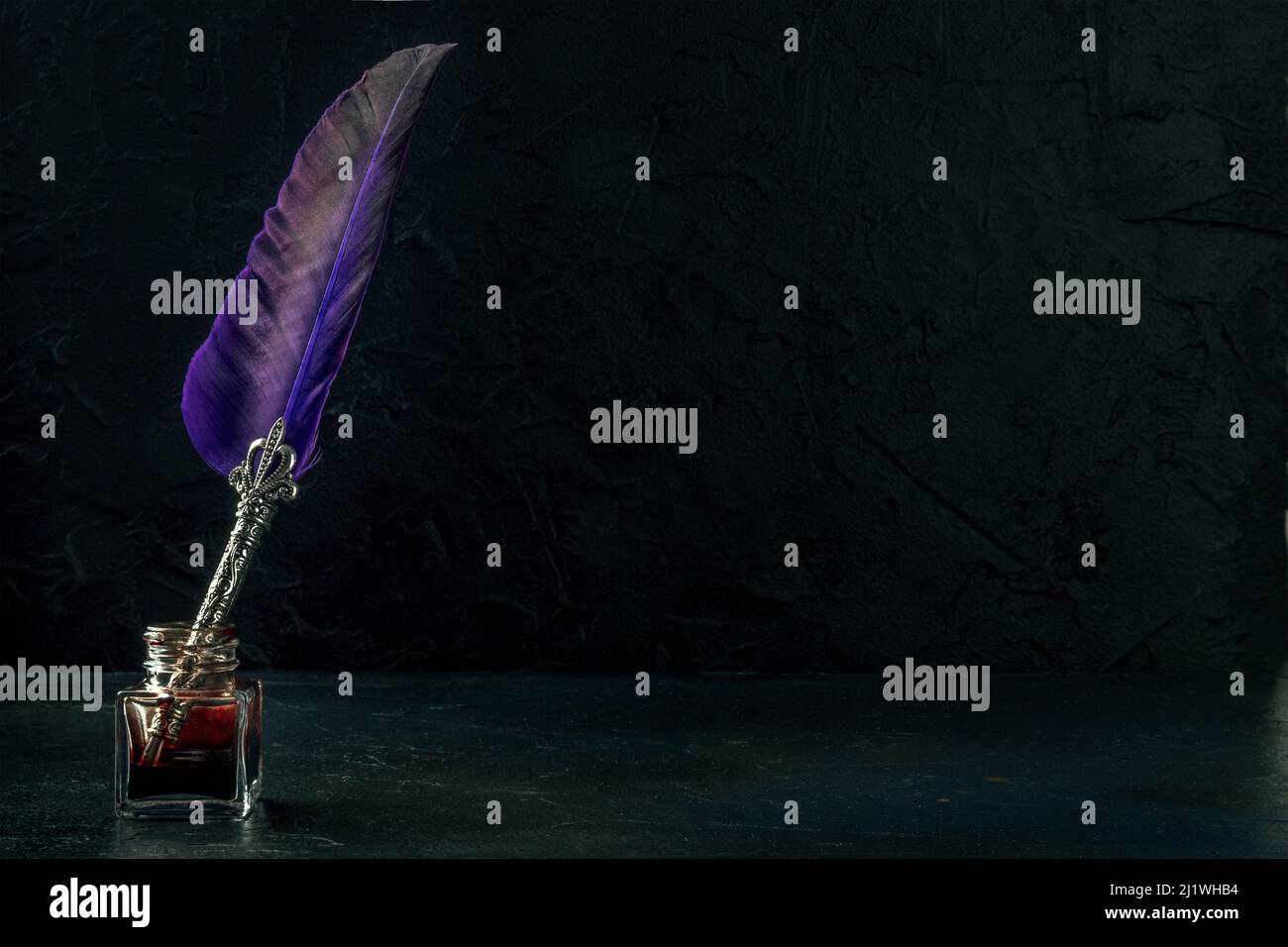 Purple quill pen with a retro ink well, a side view on a dark ...