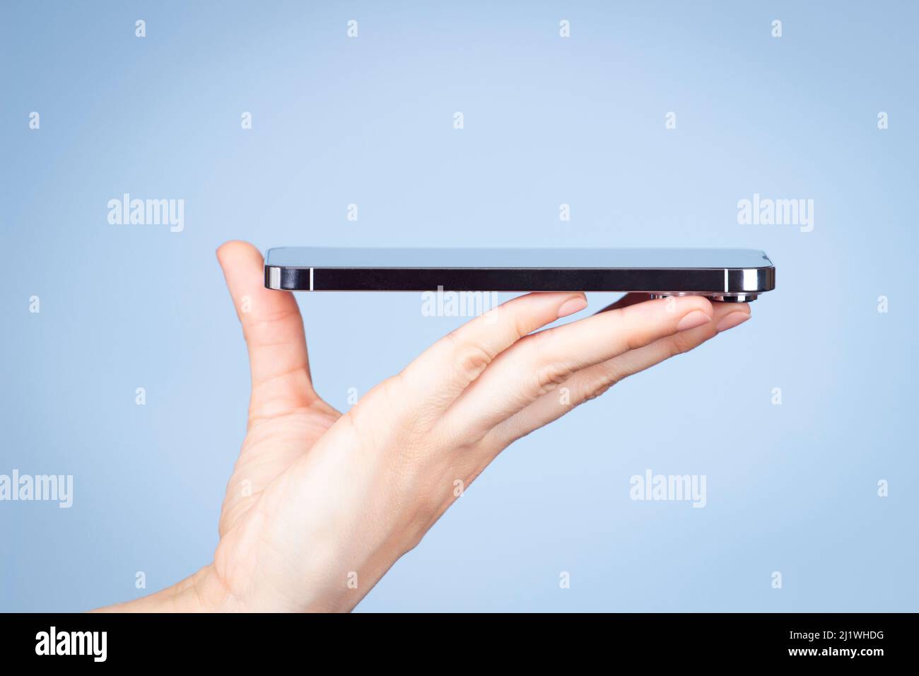 Woman hand holding smartphone screen face up side view on light blue ...