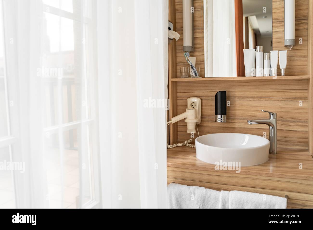 Bathroom in hotel room with window, sink, faucet, face care set and ...