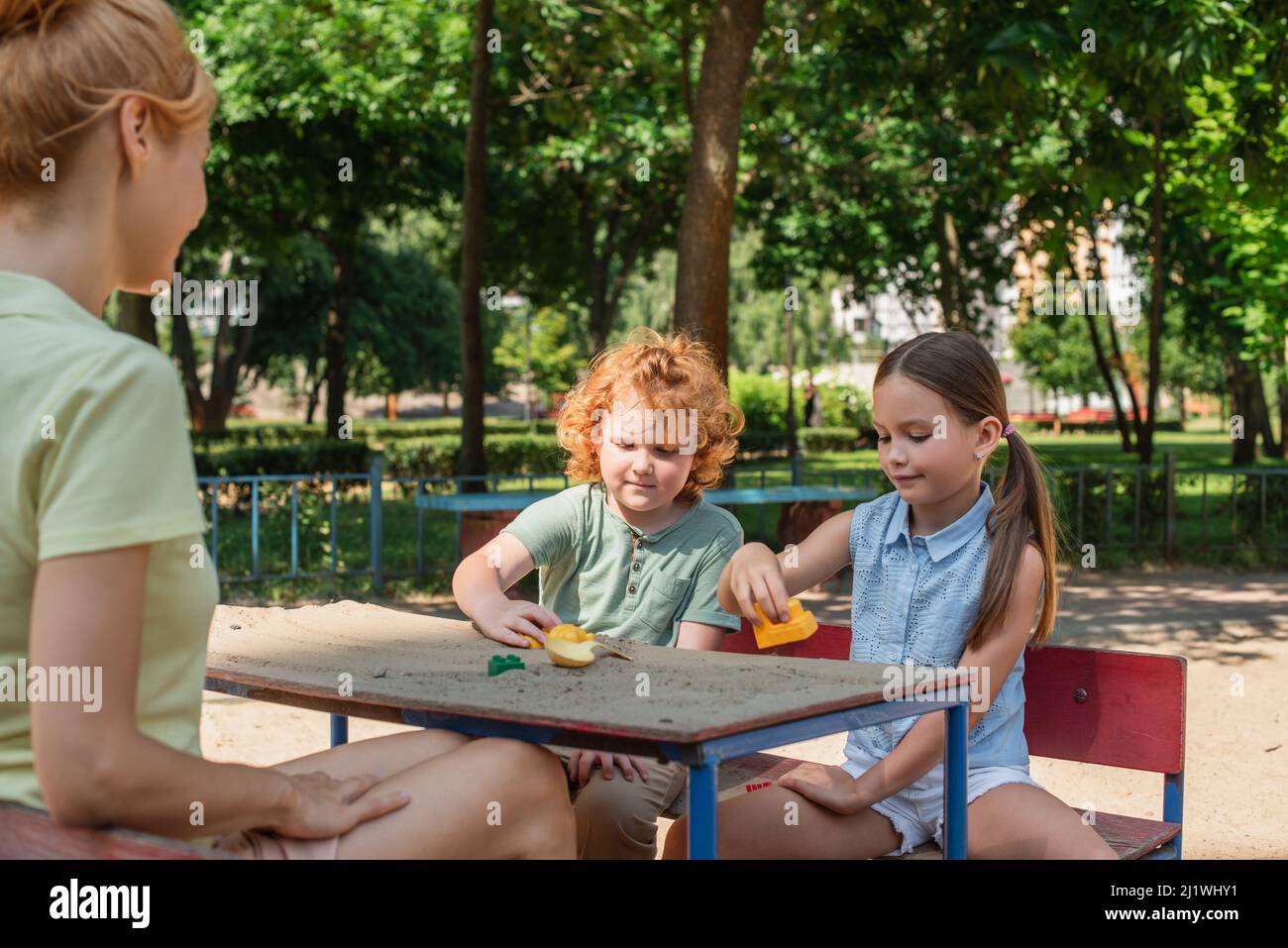 kids playing with toys and sand while sitting near mother on playground ...