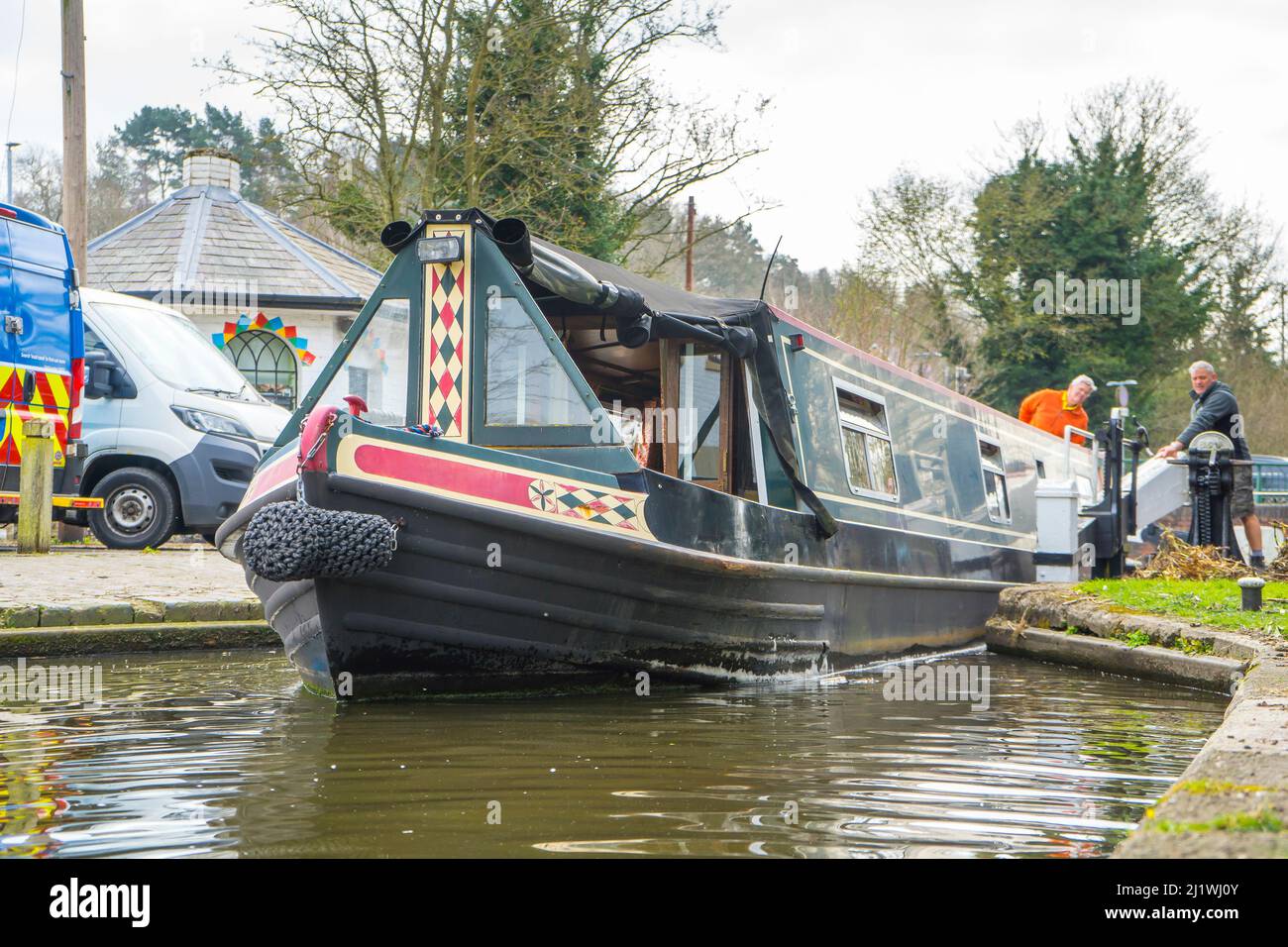 Close up of narrowboat passing through open lock on UK canal with man ...
