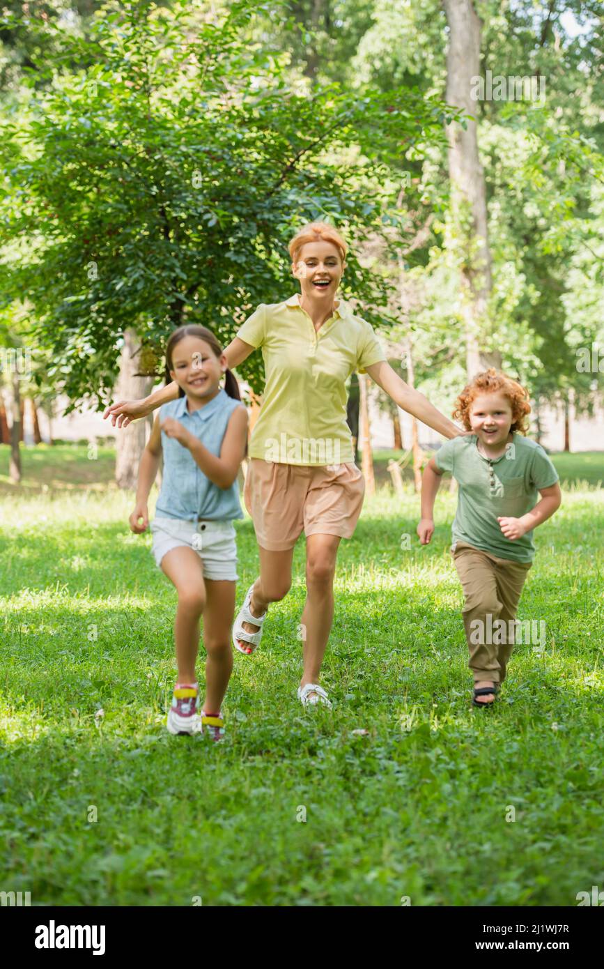 full length view of excited children with mother running in summer park ...