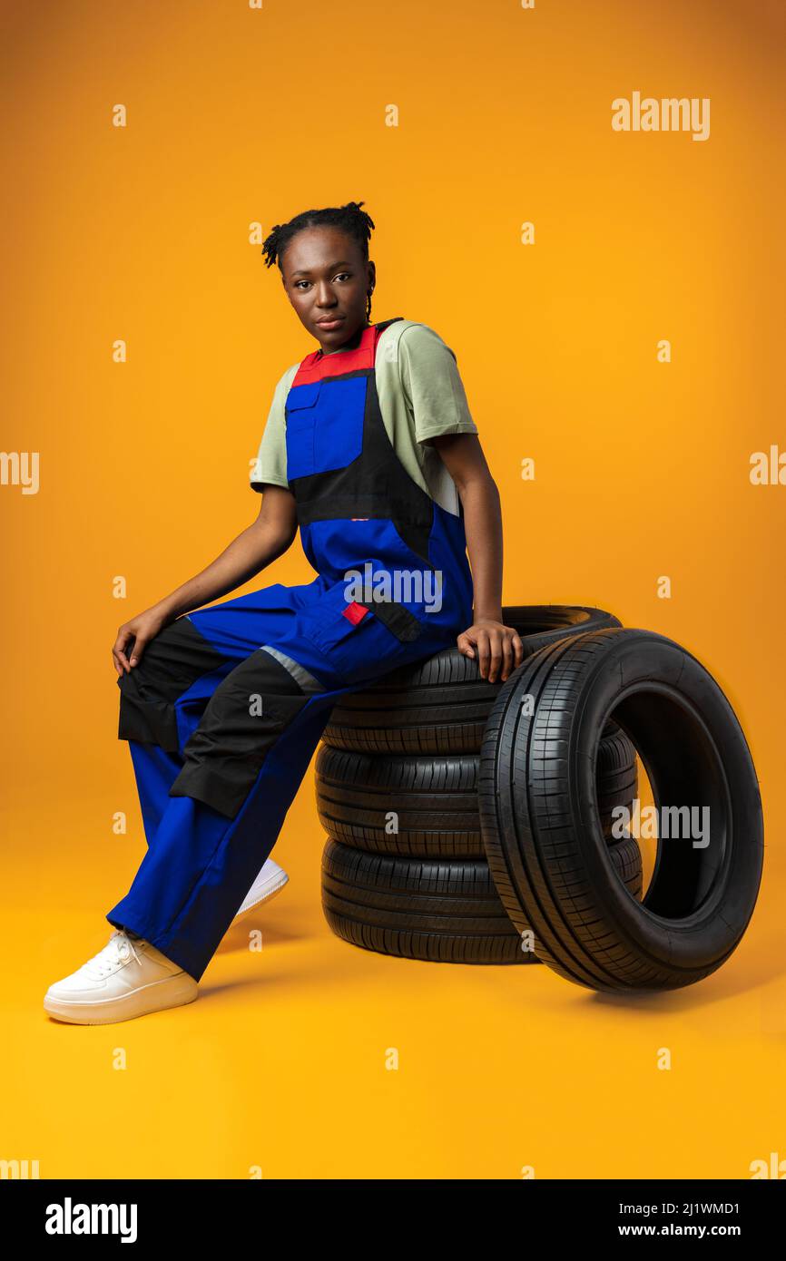 Portrait of smiling black female mechanic posing with new car tyres in ...