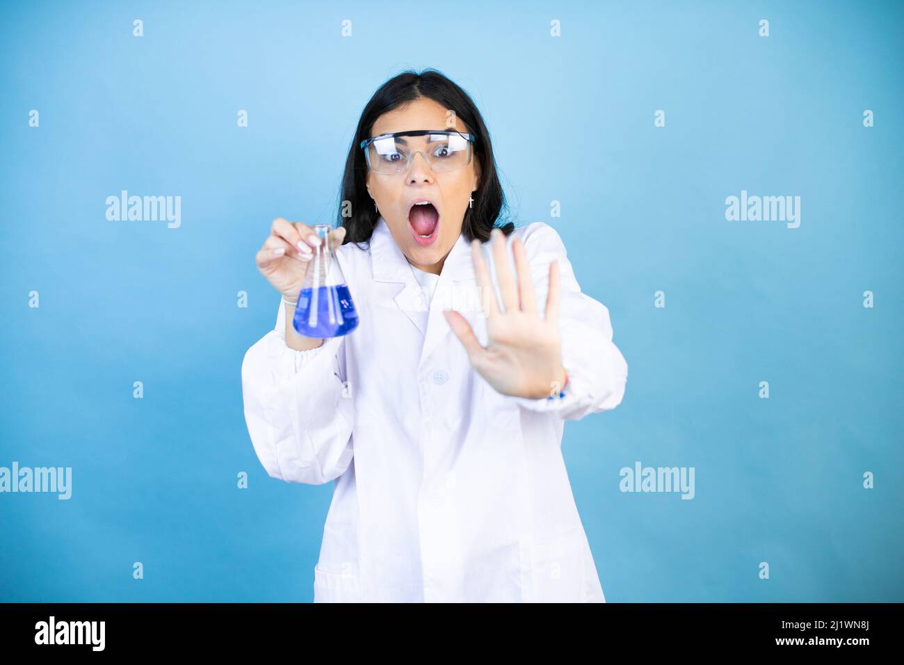 Young brunette woman wearing scientist uniform holding test tube over ...