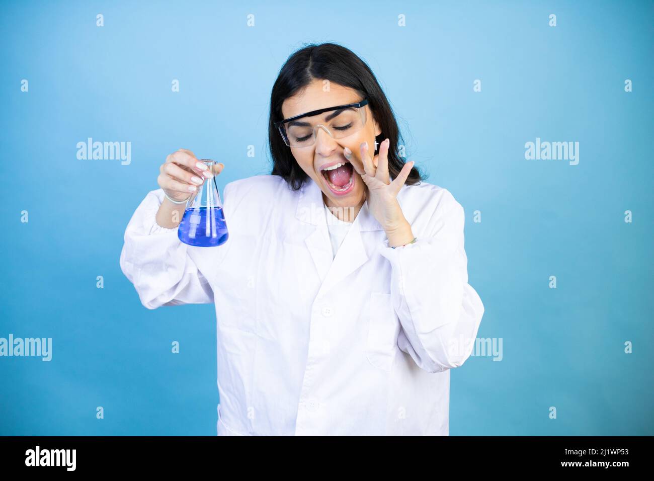 Young brunette woman wearing scientist uniform holding test tube over ...