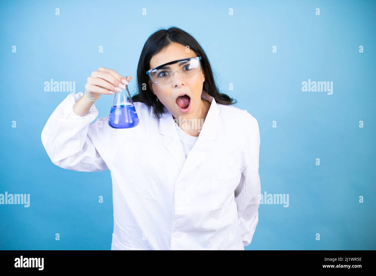 Young brunette woman wearing scientist uniform holding test tube over ...