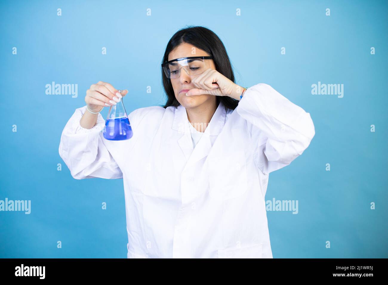 Young brunette woman wearing scientist uniform holding test tube over ...