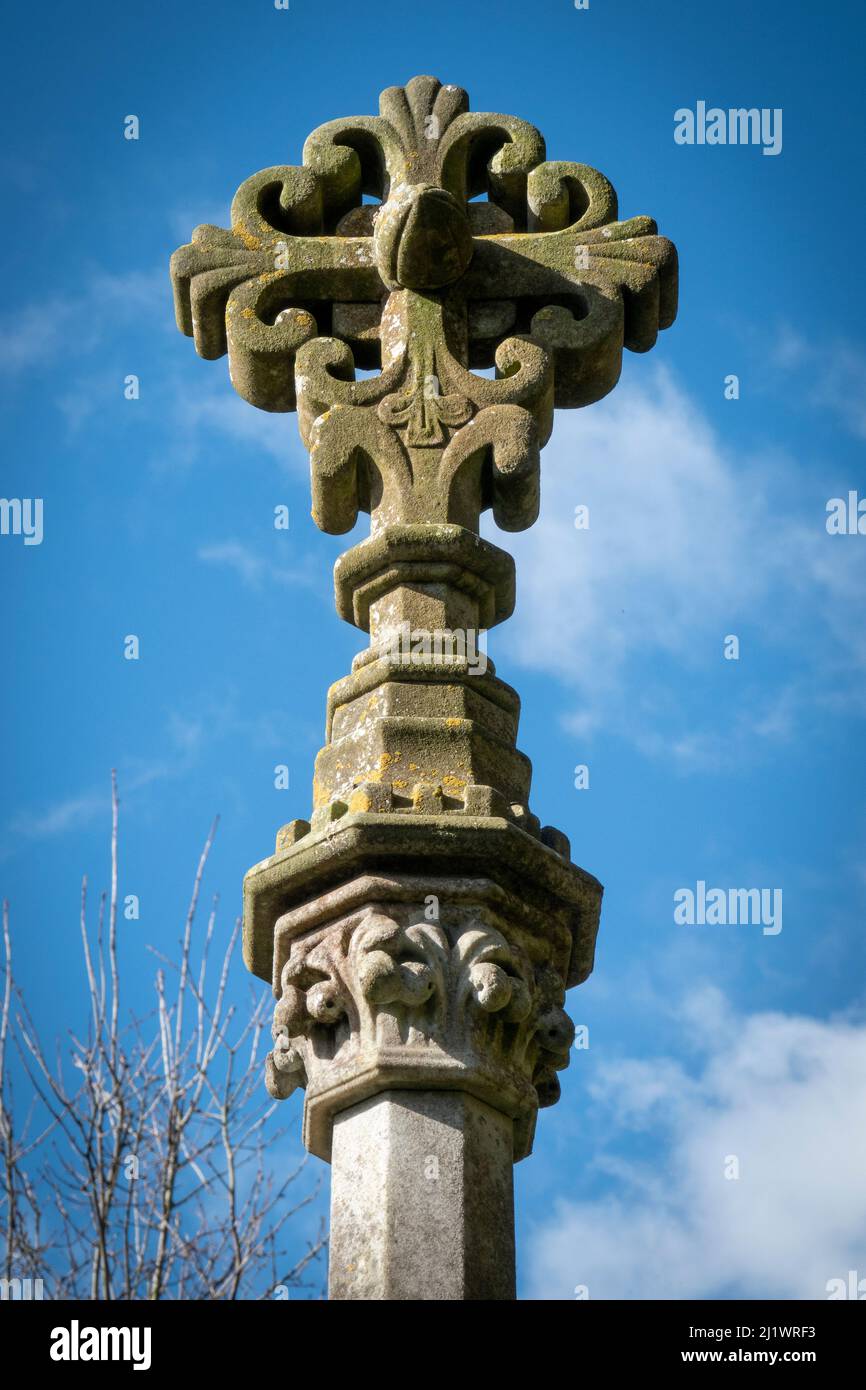 Ornate stone carved cross on a narrow stone column against a blue sky ...