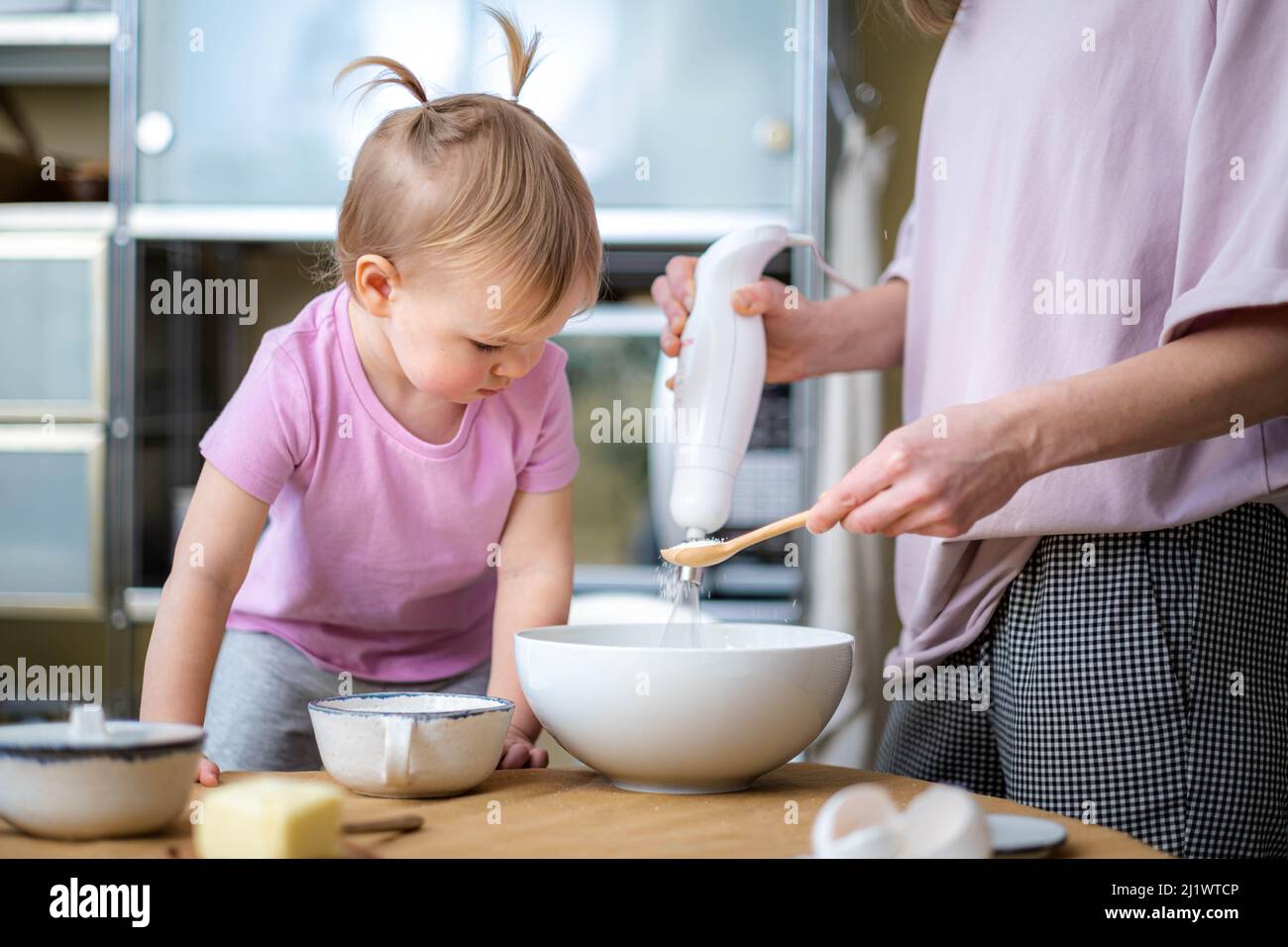 Little cute funny girl helping mother prepare pie cake in kitchen ...