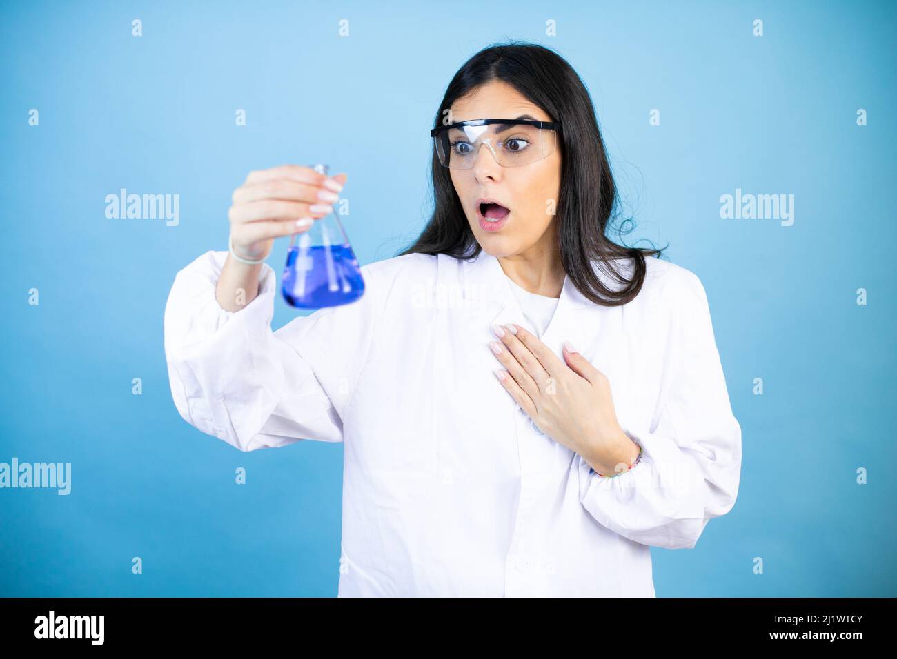 Young brunette woman wearing scientist uniform holding test tube over ...