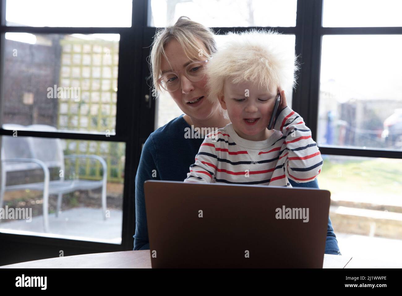 A mother working from home at a laptop computer with her young son on ...