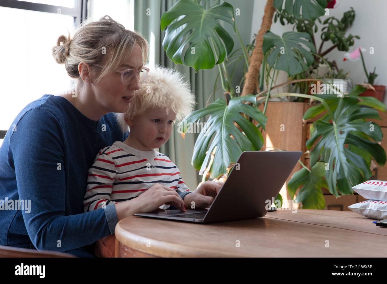 A Mother Working From Home At A Laptop Computer With Her Young Son On