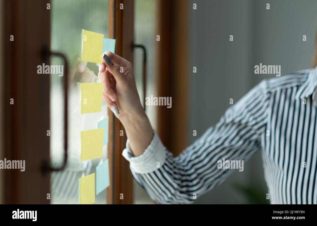 Young creative woman professional using sticky notes in glass wall to ...