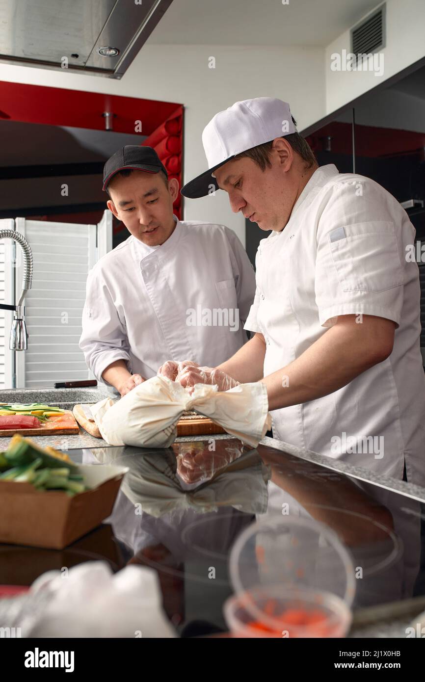 Two happy young asian chefs dressed in white uniform preparing ...