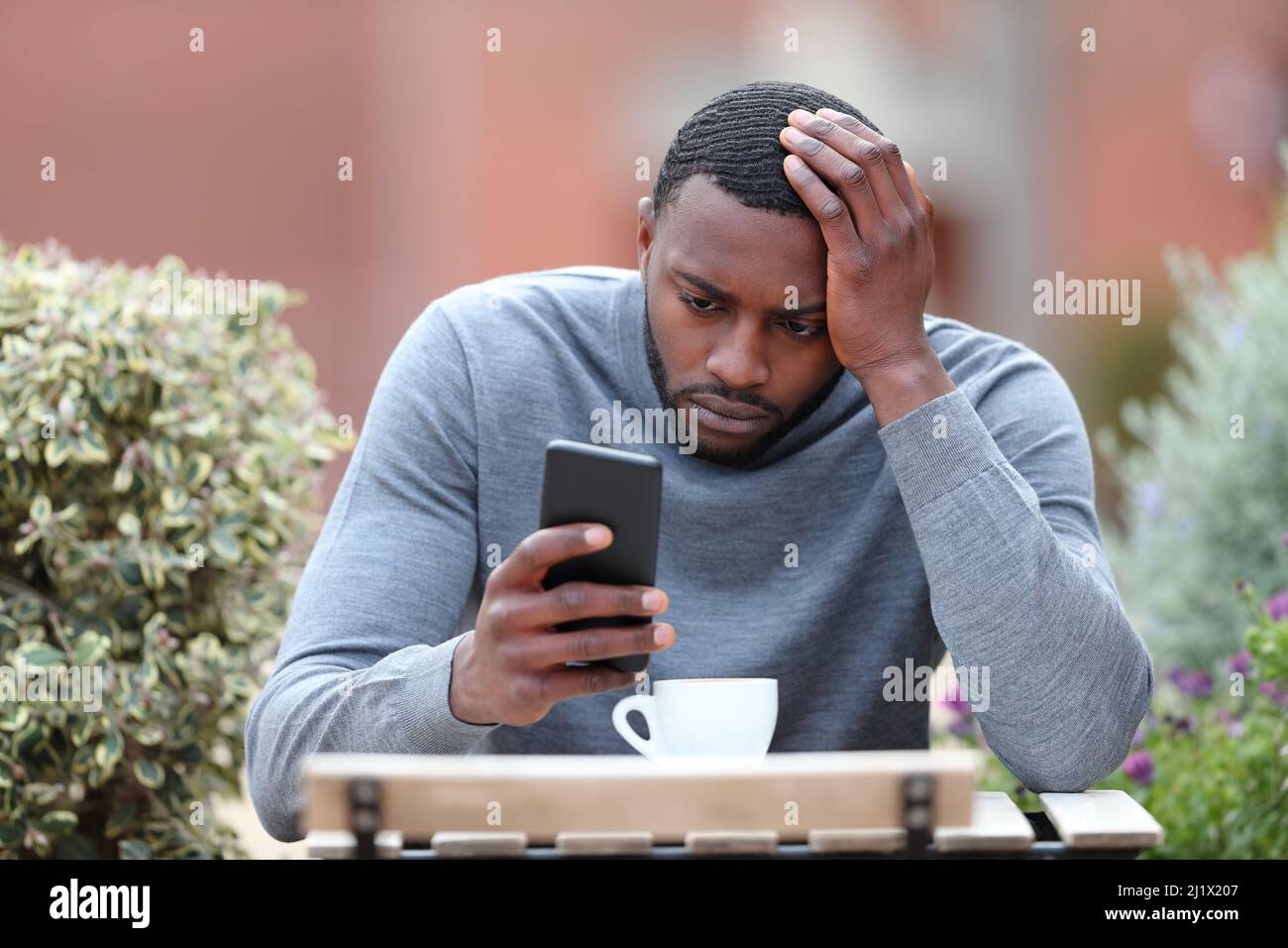Front view portrait of a worried man with black skin checking phone in a coffee shop Stock Photo ...