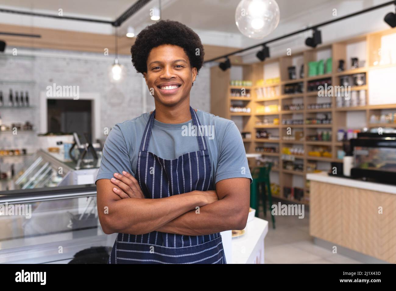 Portrait of smiling african american young male barista with arms ...