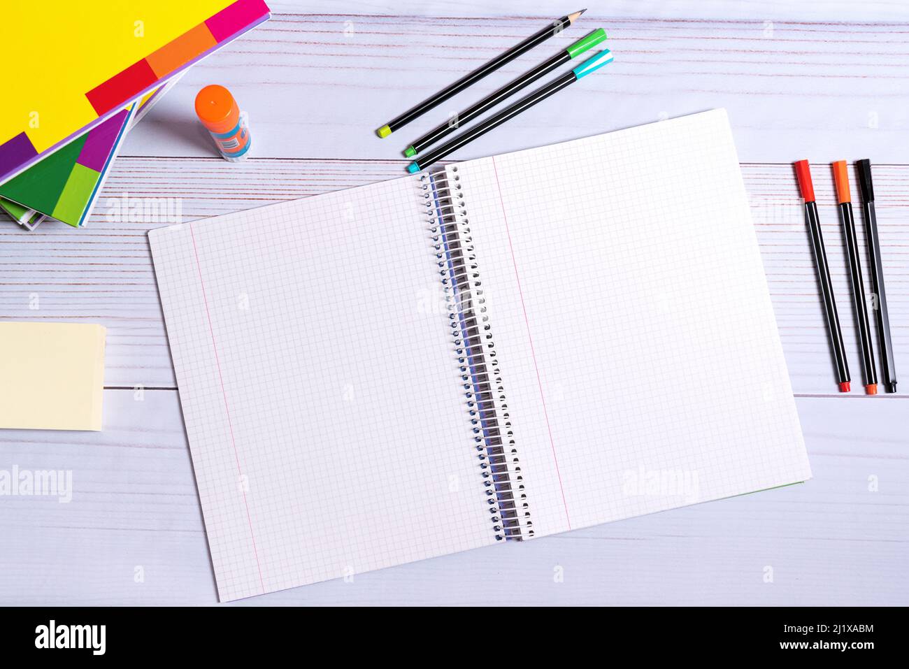 SCHOOL SUPPLIES. BOOK TILTED AND OPEN. NOTEBOOK, COLORED PENS. STACKED ...