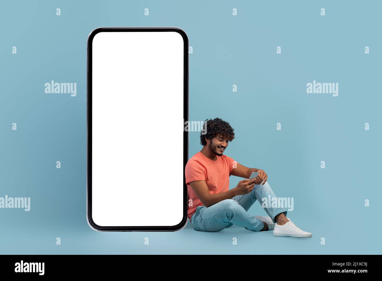 Rlaxed young indian man using cell phone, sitting on blue Stock Photo ...