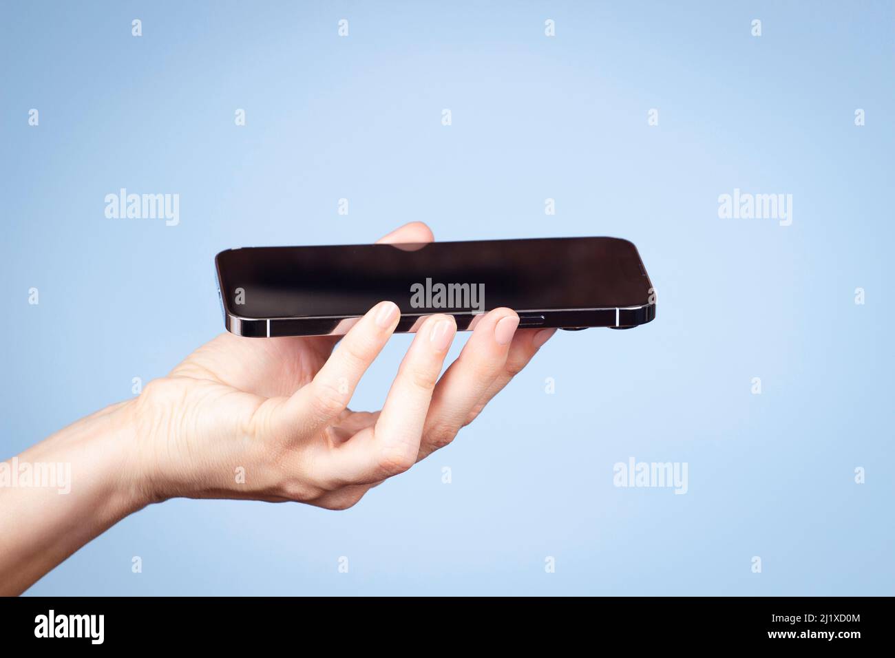 Woman hand holding smartphone screen face up side view on light blue ...