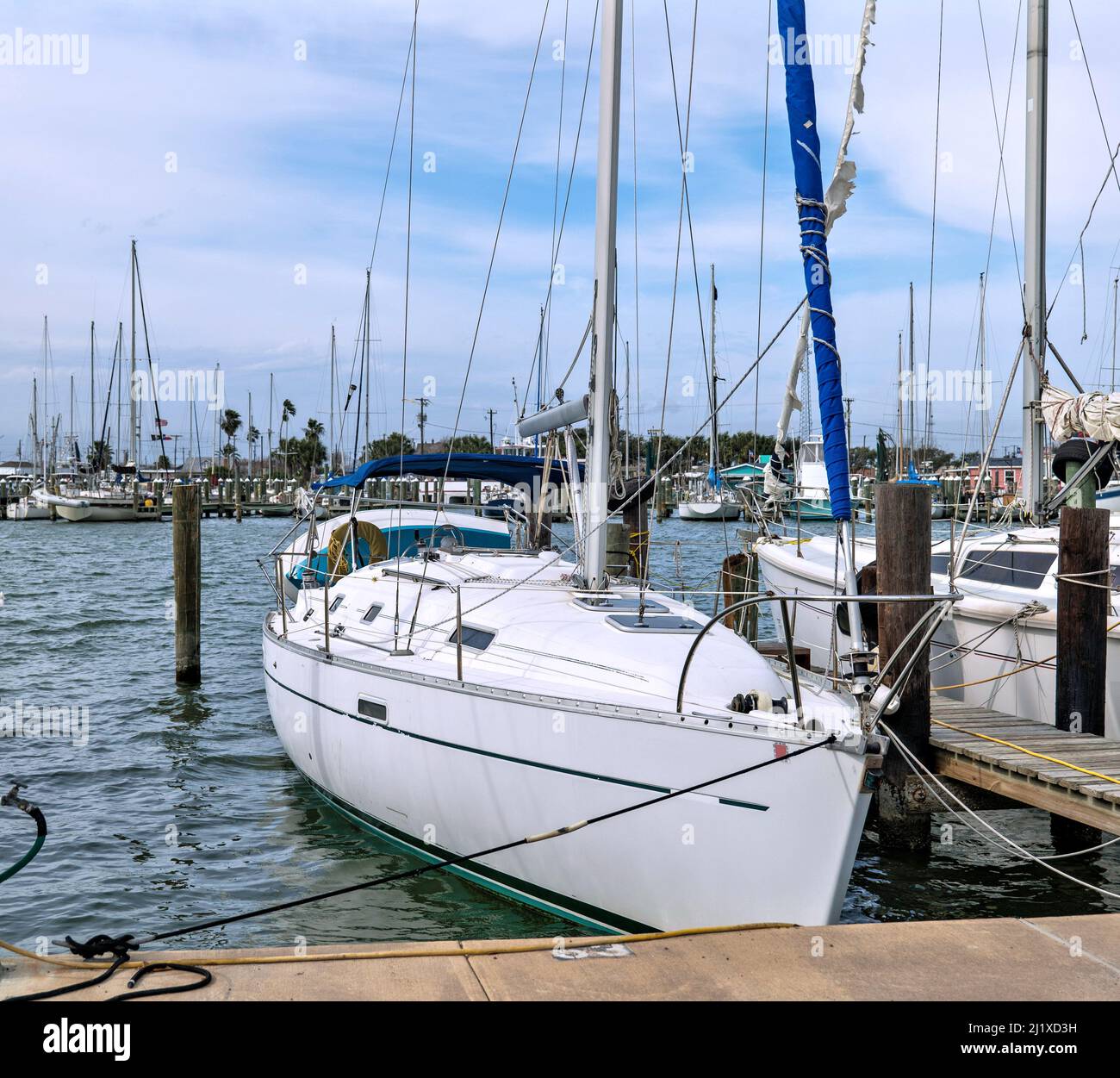White sailboat with mast and rigging is tied to the dock in a marina by ...