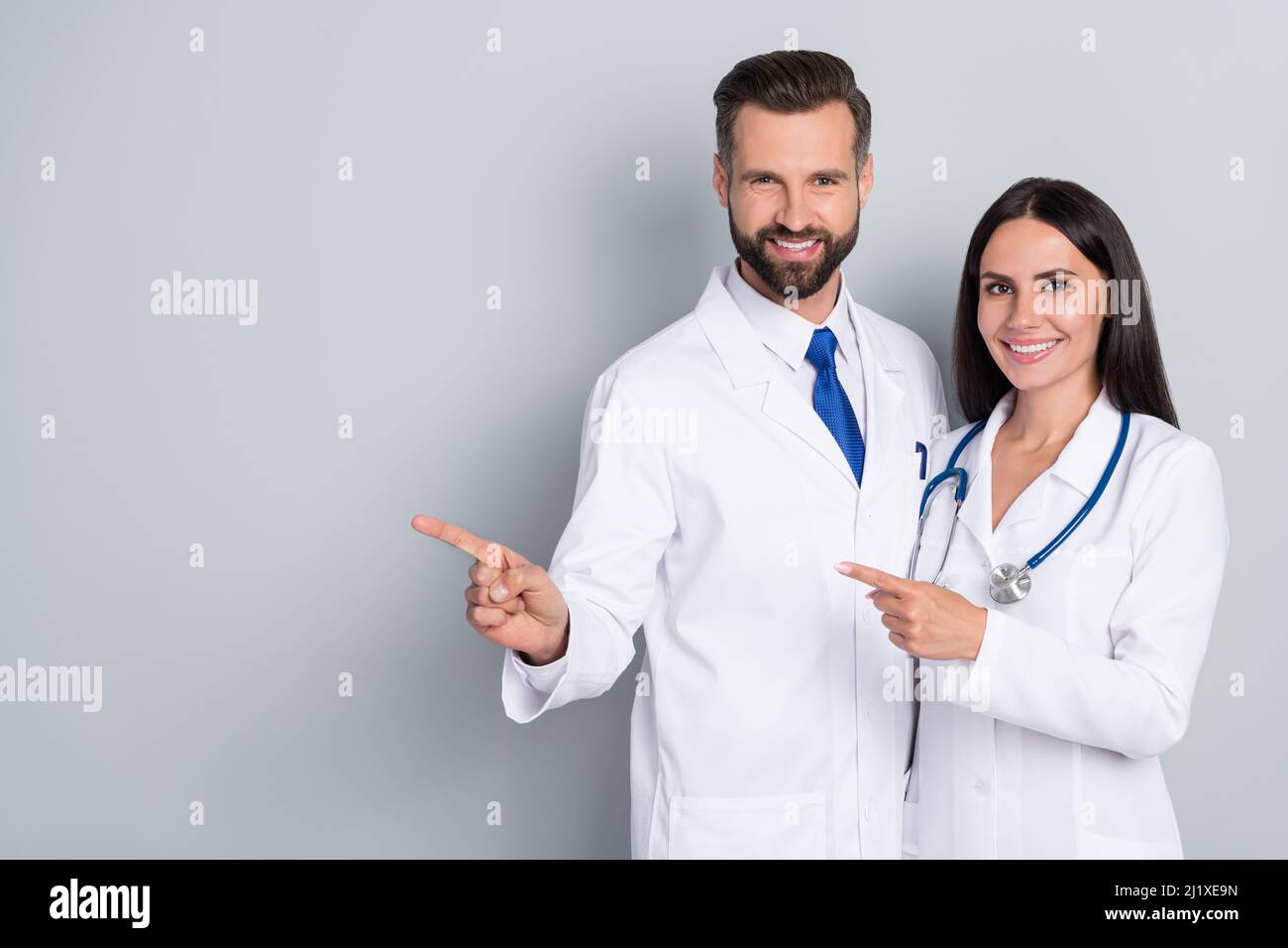 Photo of positive pretty two doctors wear white coats pointing empty ...