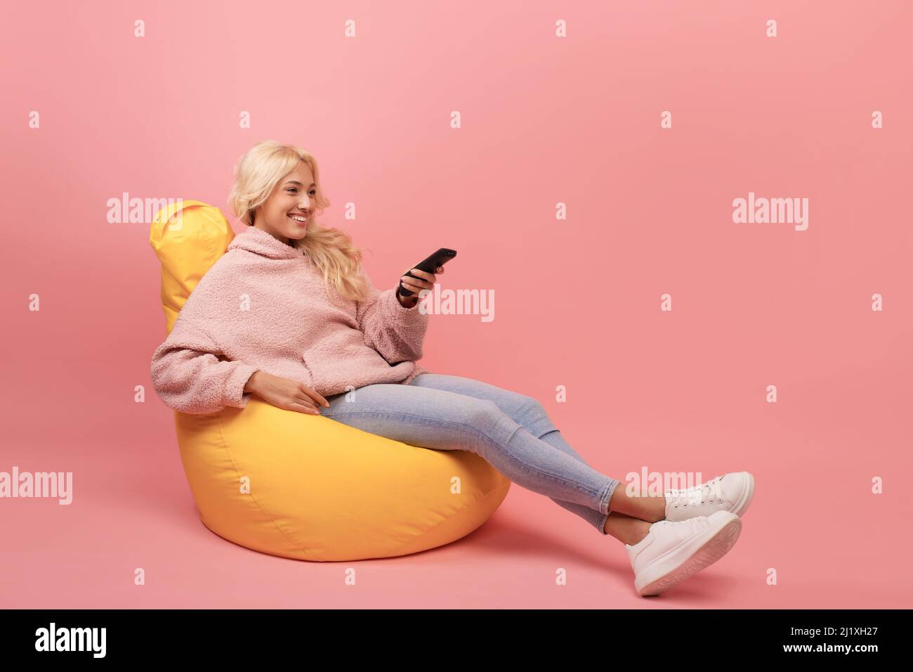 Television programming. Happy lady with remote control sitting in ...