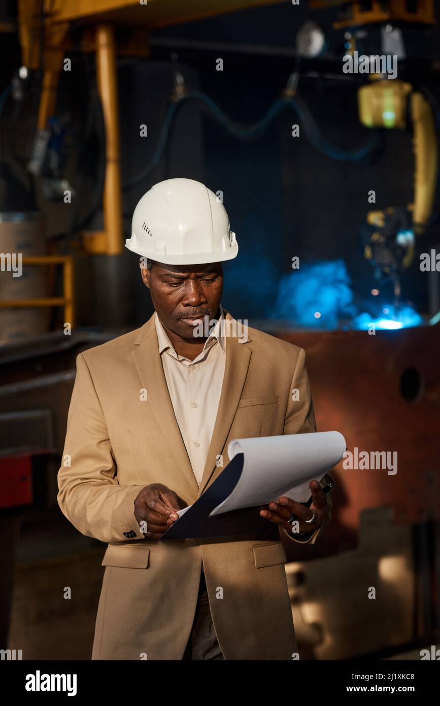 Serious foreman in work helmet reading manufacturing plan while ...