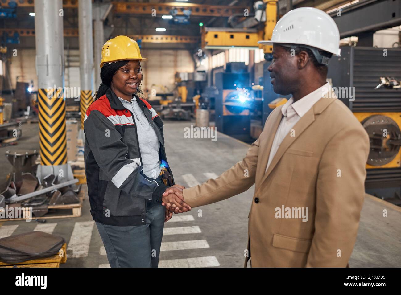 African manager in suit shaking hands with female worker in uniform to ...