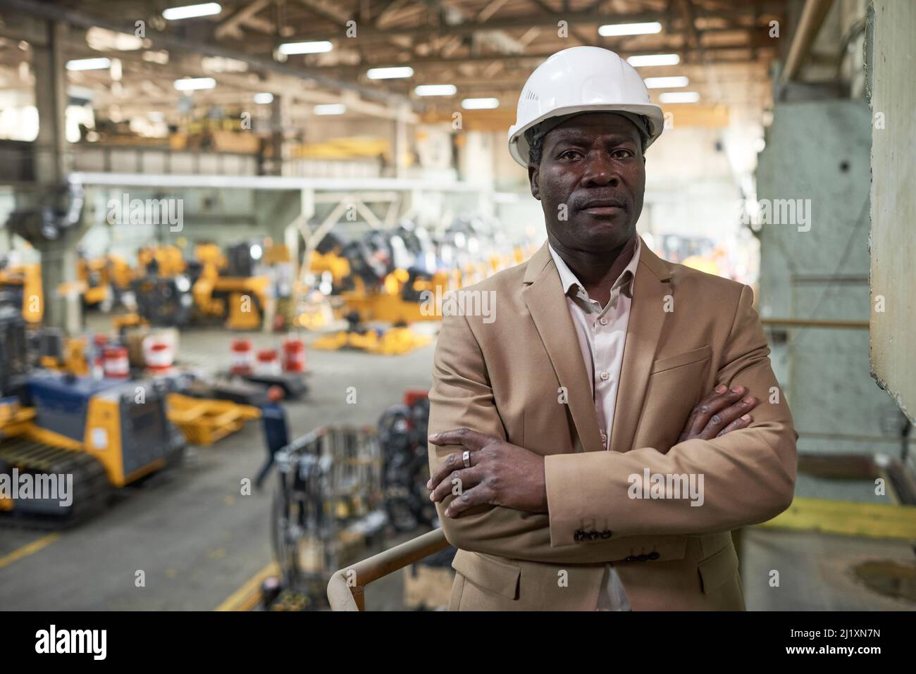 Portrait of African engineer in work helmet standing with arms crossed ...